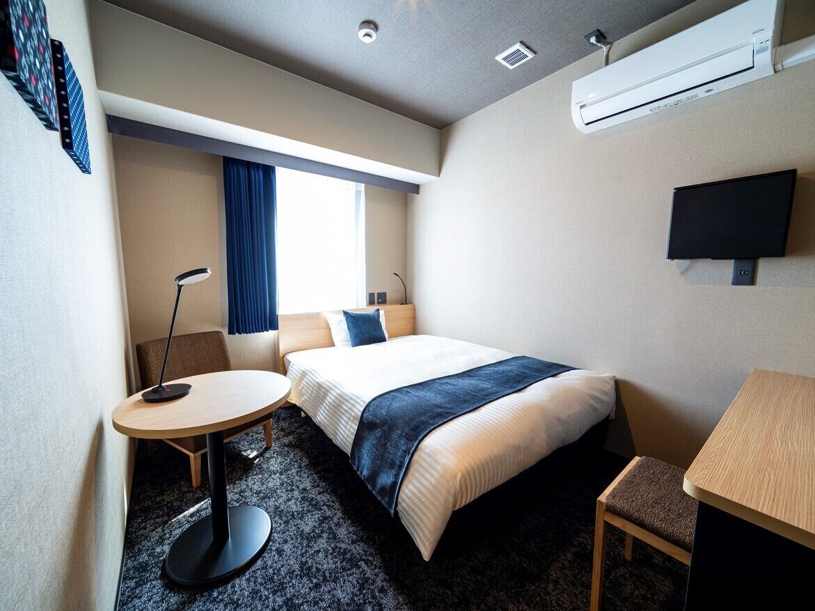 Quarto de hotel com cama, escrivaninha, cadeira, mesa redonda, televisão e ar condicionado.