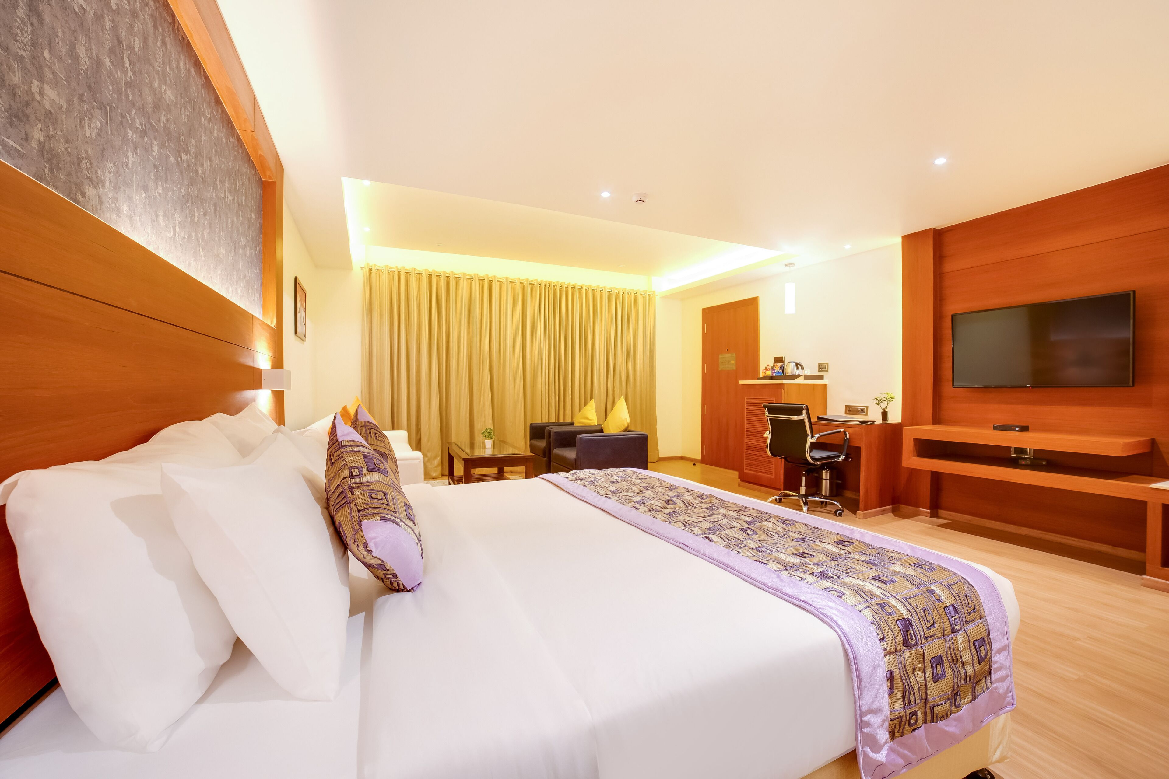 Quarto de hotel com uma cama grande, uma escrivaninha, uma cadeira, uma TV e uma parede de madeira.
