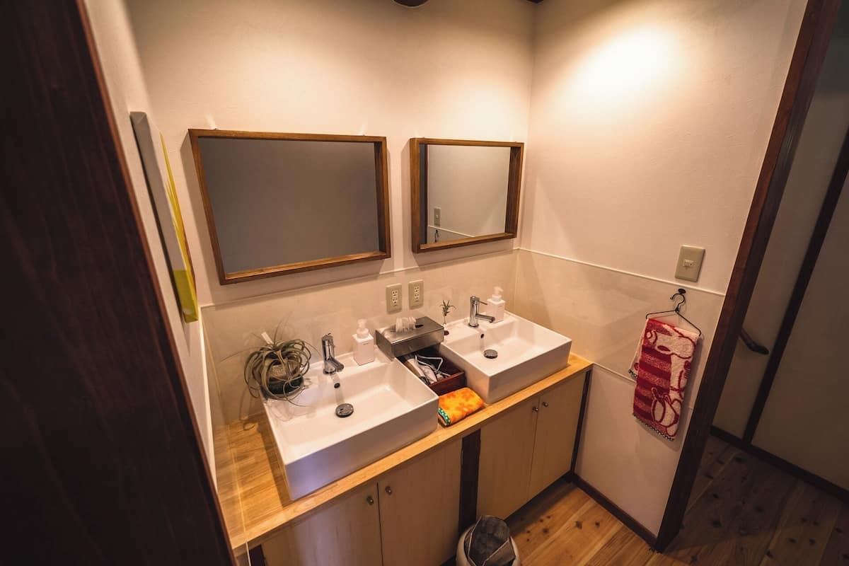 Casa de banho com duas pias, espelhos, porta-toalhas e um pequeno cesto de lixo.