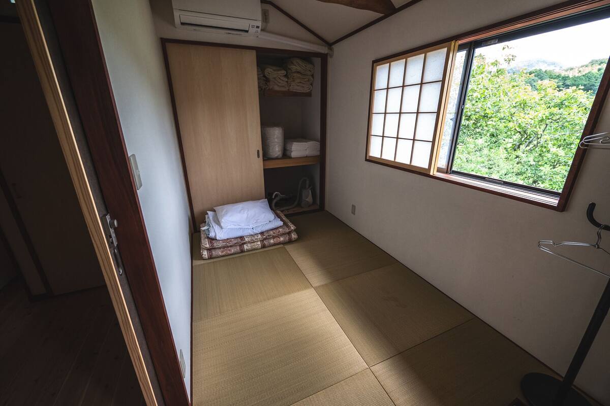 Quarto compacto com tatame, janela com portas shoji, guarda-roupa e uma cama pequena.