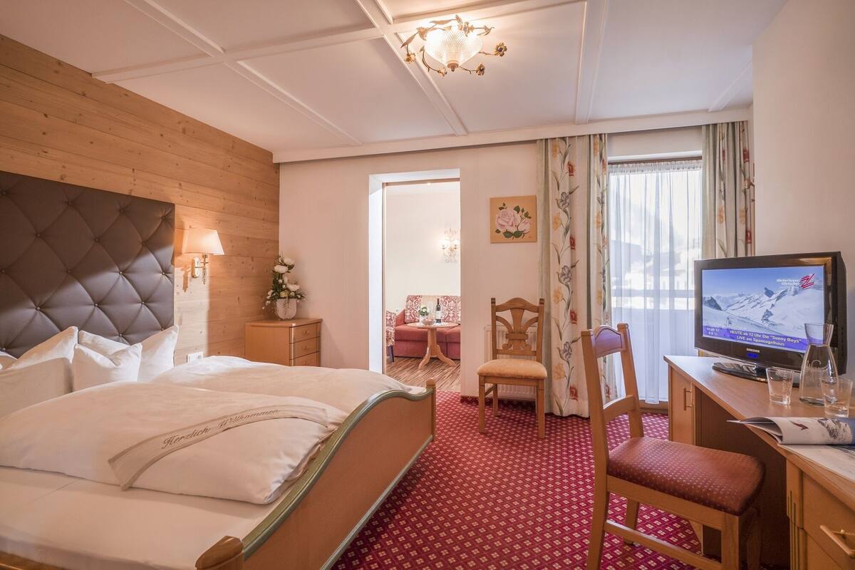 Quarto de hotel com cama, escrivaninha com computador, cadeira e televisão.