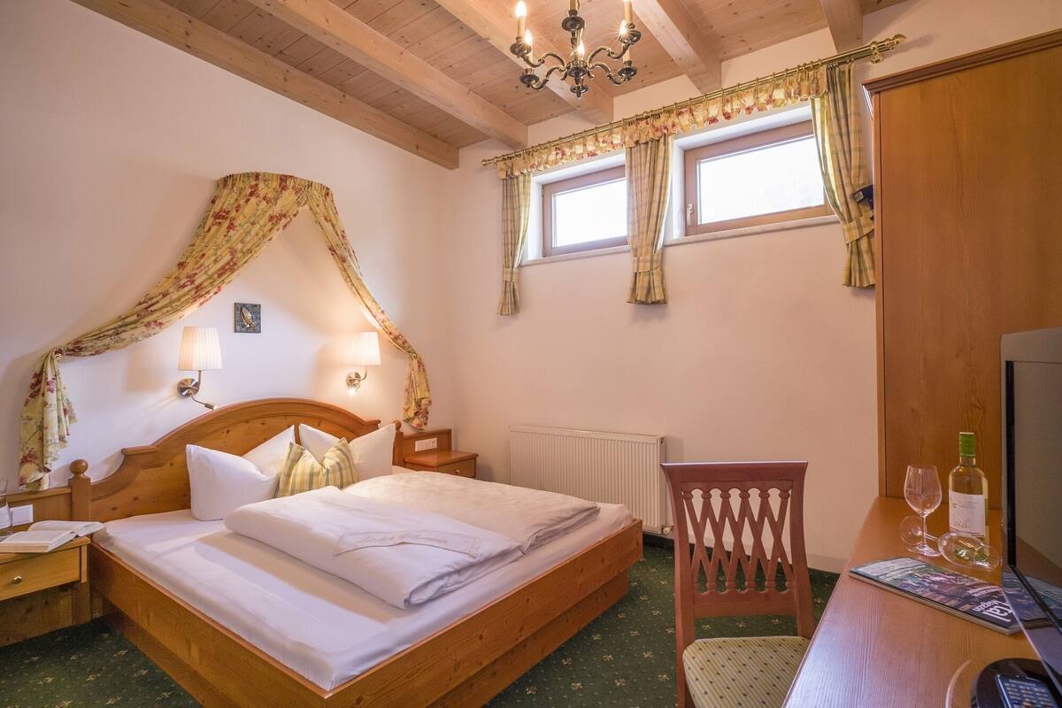 Quarto com cama de madeira, mesa de cabeceira, cadeira, radiador e televisão.
