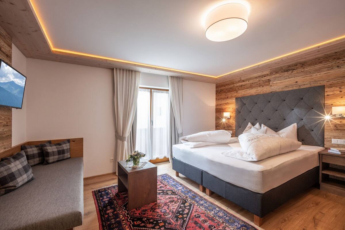Quarto moderno com uma cama grande, um sofá, uma televisão e teto de madeira.