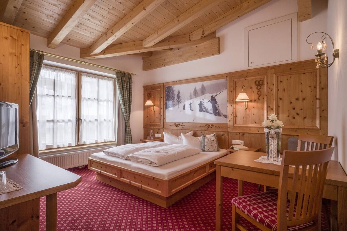 Quarto de madeira com cama, escrivaninha, cadeira e um quadro na parede.