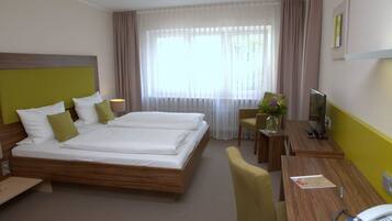 Quarto de hotel com cama de casal, escrivaninha com telefone, cadeira e televisão.