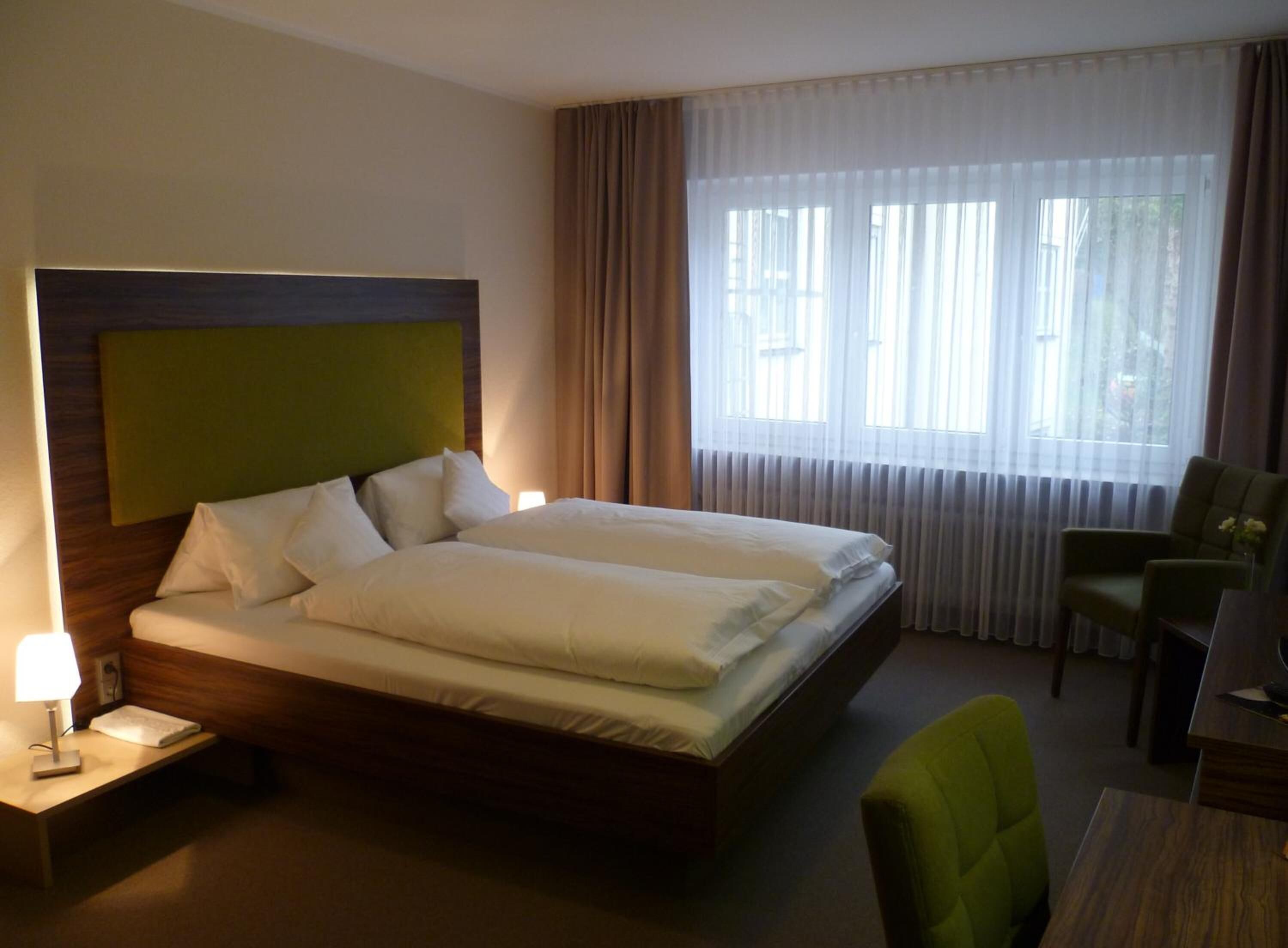 Quarto de hotel com uma cama grande, mesa de cabeceira, escrivaninha e uma cadeira.