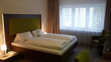 Quarto de hotel com uma cama grande, mesa de cabeceira, escrivaninha e uma cadeira.