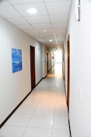 Um corredor comprido e estreito com paredes brancas, chão de azulejos e portas em ambos os lados.