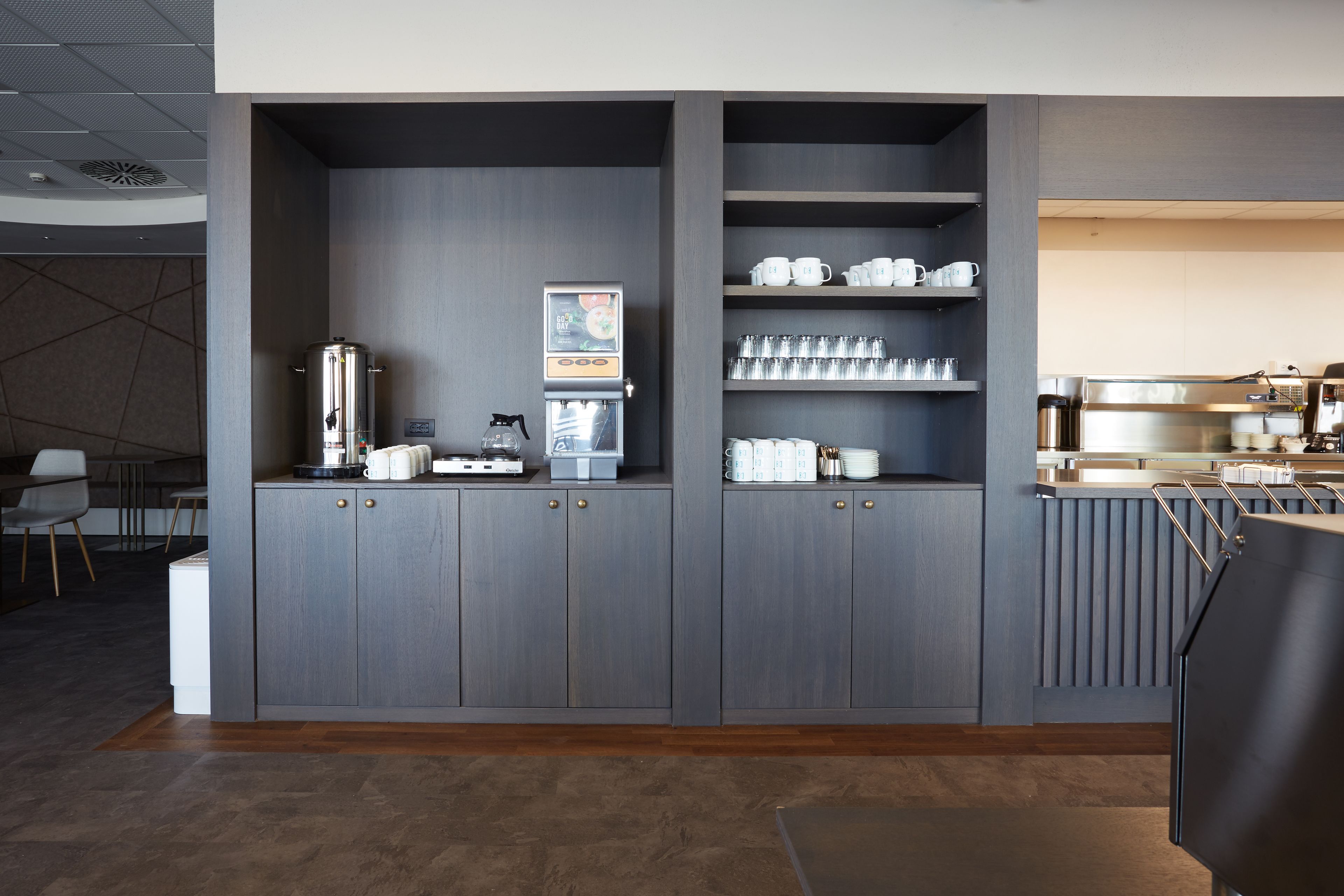 Cozinha moderna com eletrodomésticos embutidos, incluindo máquina de café e chaleira, e prateleiras com xícaras e pratos.