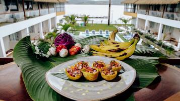 Uma mesa com um prato de aperitivos, uma banana e uma tigela de frutas sobre uma folha.