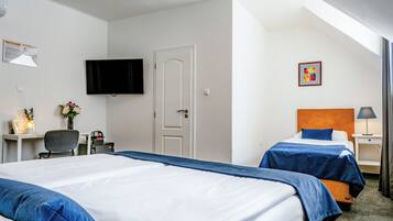 Quarto de hotel com duas camas, uma escrivaninha, uma cadeira, uma televisão e uma porta.