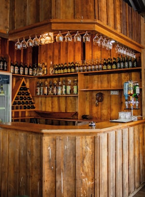 Um balcão de madeira com prateleiras de garrafas de bebidas, um suporte para vinhos e um caixa registradora.
