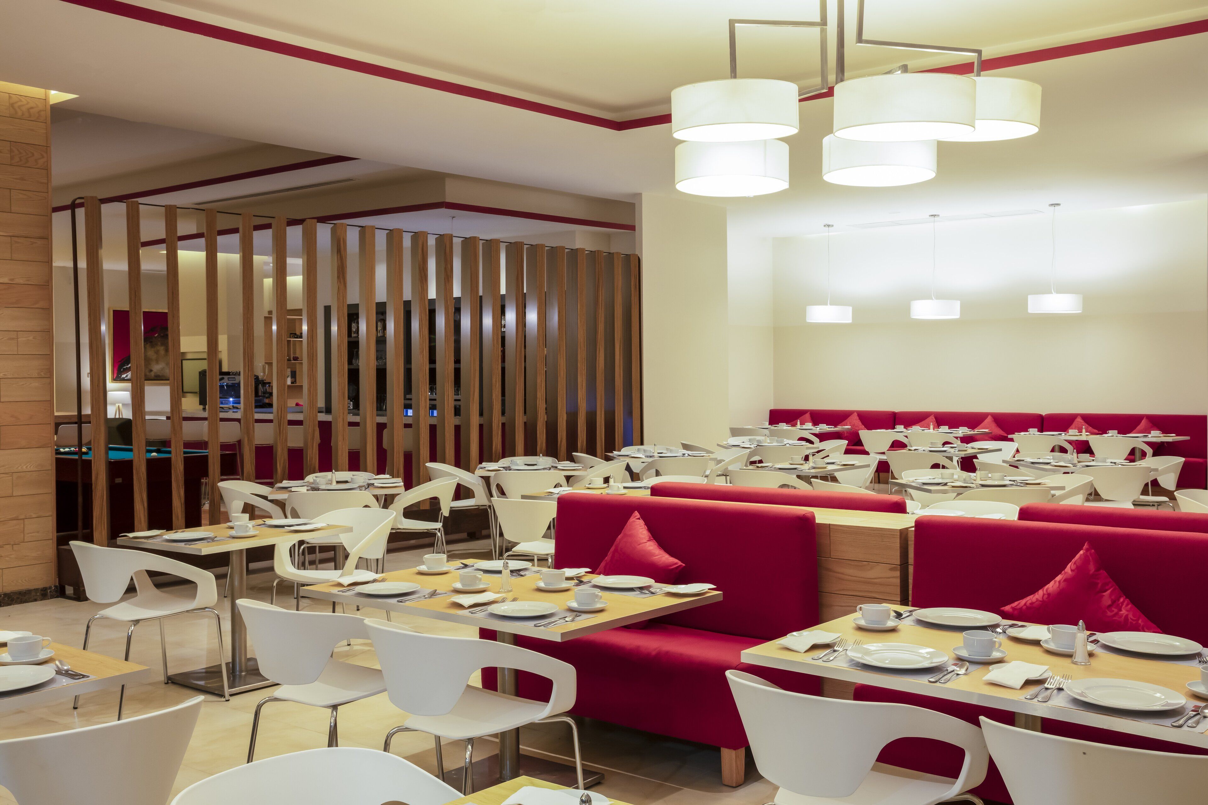 Restaurante com bancos vermelhos, cadeiras brancas e mesas preparadas para refeições.