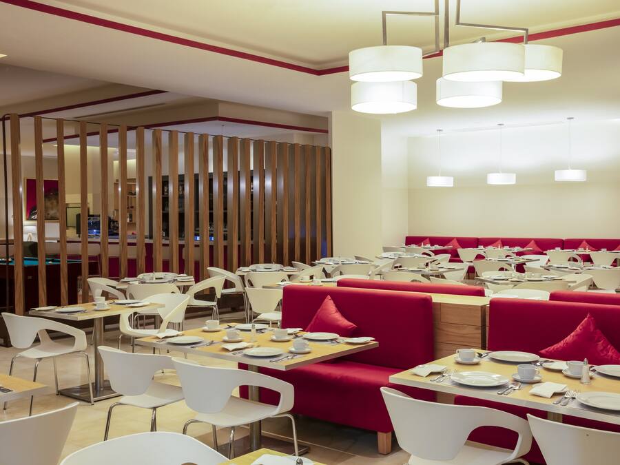 Restaurante com bancos vermelhos, cadeiras brancas e mesas preparadas para refeições.