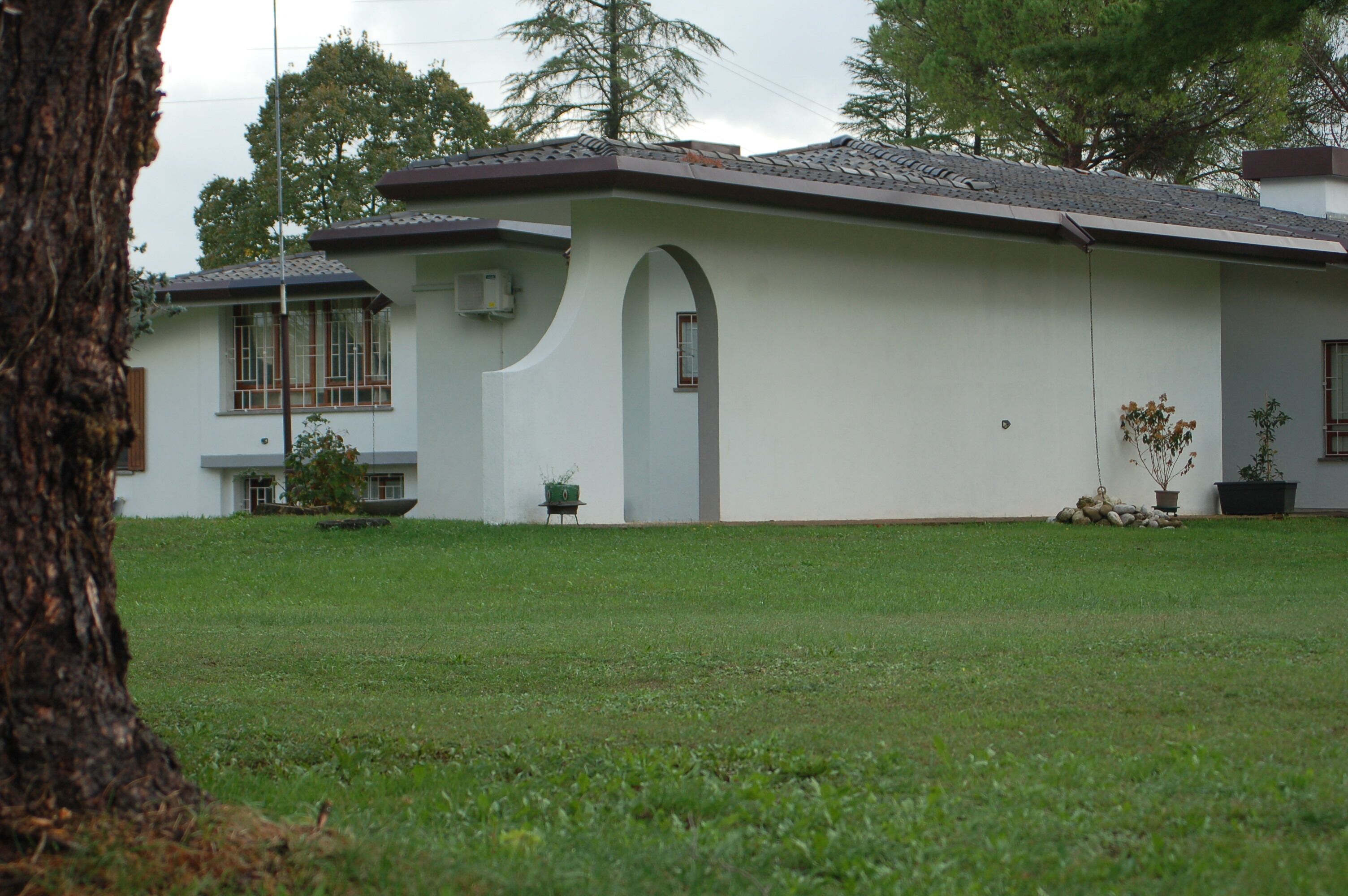 Uma casa térrea com telhado plano, uma grande porta em arco e uma pequena varanda.