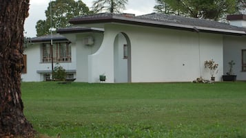 Uma casa térrea com telhado plano, uma grande porta em arco e uma pequena varanda.