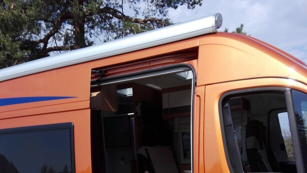 Uma motorhome Summit 600 Plus com a porta aberta, mostrando interior de madeira, um banco e uma pequena mesa.