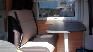 Interior compacto de uma RV com cozinha compacta, área de refeições e janela com vista panorâmica.