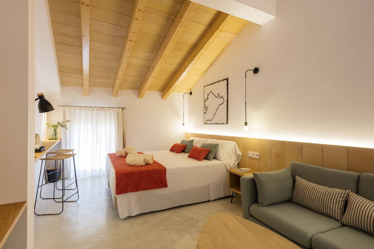 Quarto com cama, escrivaninha, sofá e janela com cortinas.
