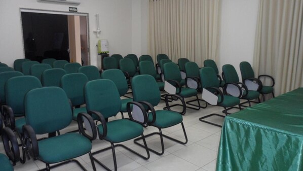 Sala de conferências com fileiras de cadeiras verdes e uma mesa coberta com um tecido verde.