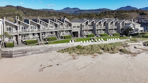 Hotel à beira-mar com várias varandas, uma praia de areia e montanhas ao fundo.