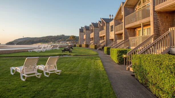 Um hotel à beira-mar com várias varandas, um gramado com espreguiçadeiras e um caminho que leva à praia.