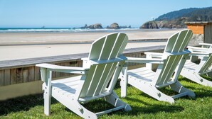 Duas cadeiras Adirondack de frente para uma praia, com um deck de madeira e uma estrutura de madeira ao fundo.