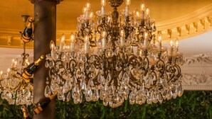 Um candelabro com várias luzes, um pilar de madeira e um sofá amarelo numa sala com painéis de madeira.