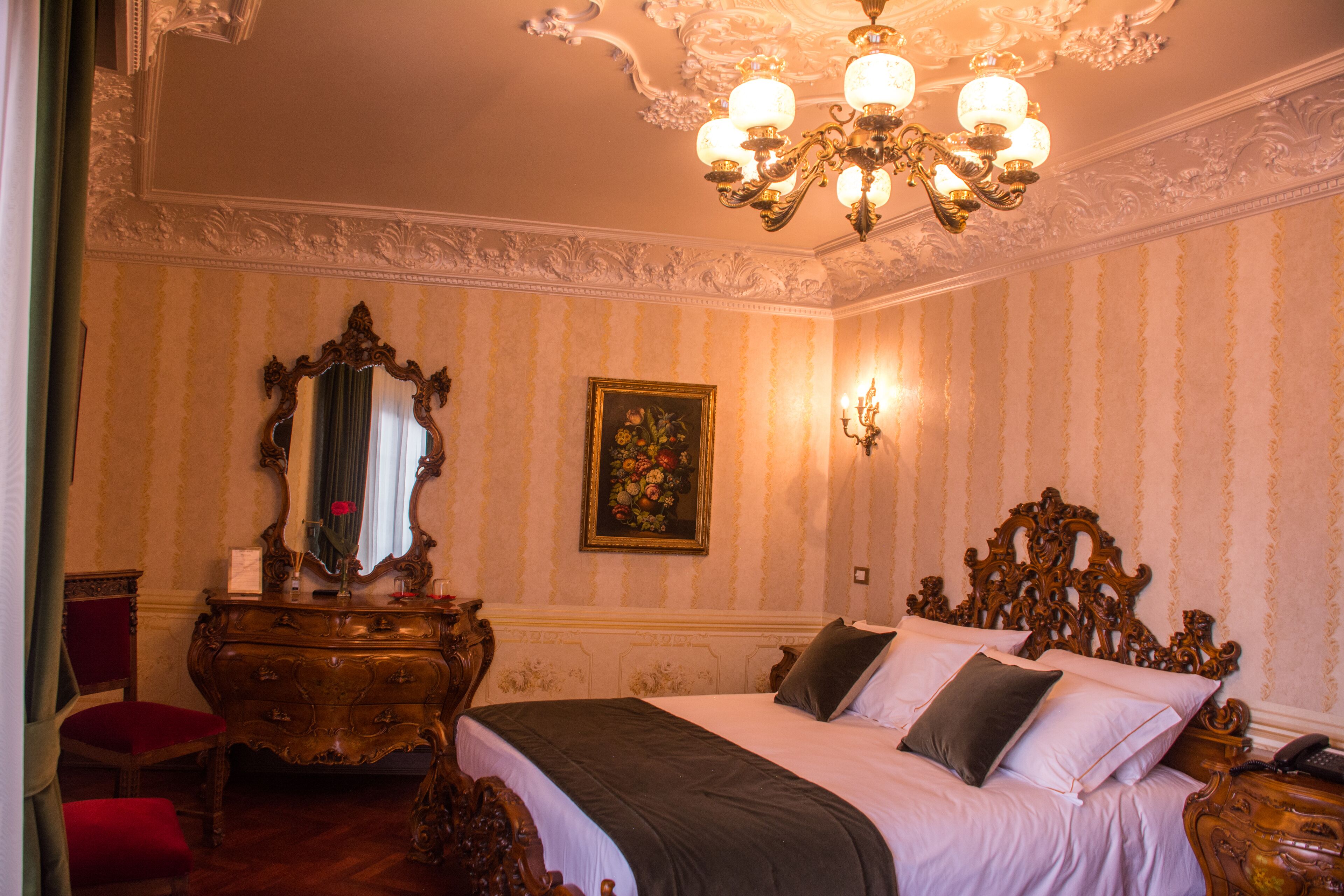 Quarto com uma cama grande, cabeceira de madeira elaborada, um aparador e um espelho.