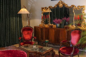 Quarto com armário de madeira, duas poltronas de veludo vermelho, uma mesa com um vaso e uma luminária.