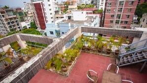 Terraço no telhado com plantas em vasos, mesa de metal e cadeiras de vime.