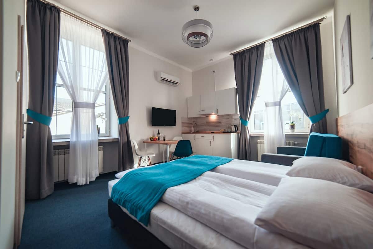 Quarto de hotel com cama, escrivaninha, cadeira, televisão e cozinha compacta.