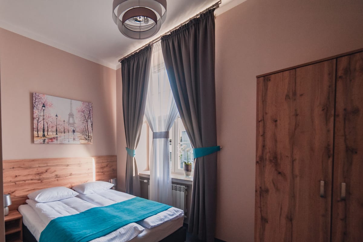 Um quarto com cama, guarda-roupa de madeira, janela com cortinas e um quadro na parede.
