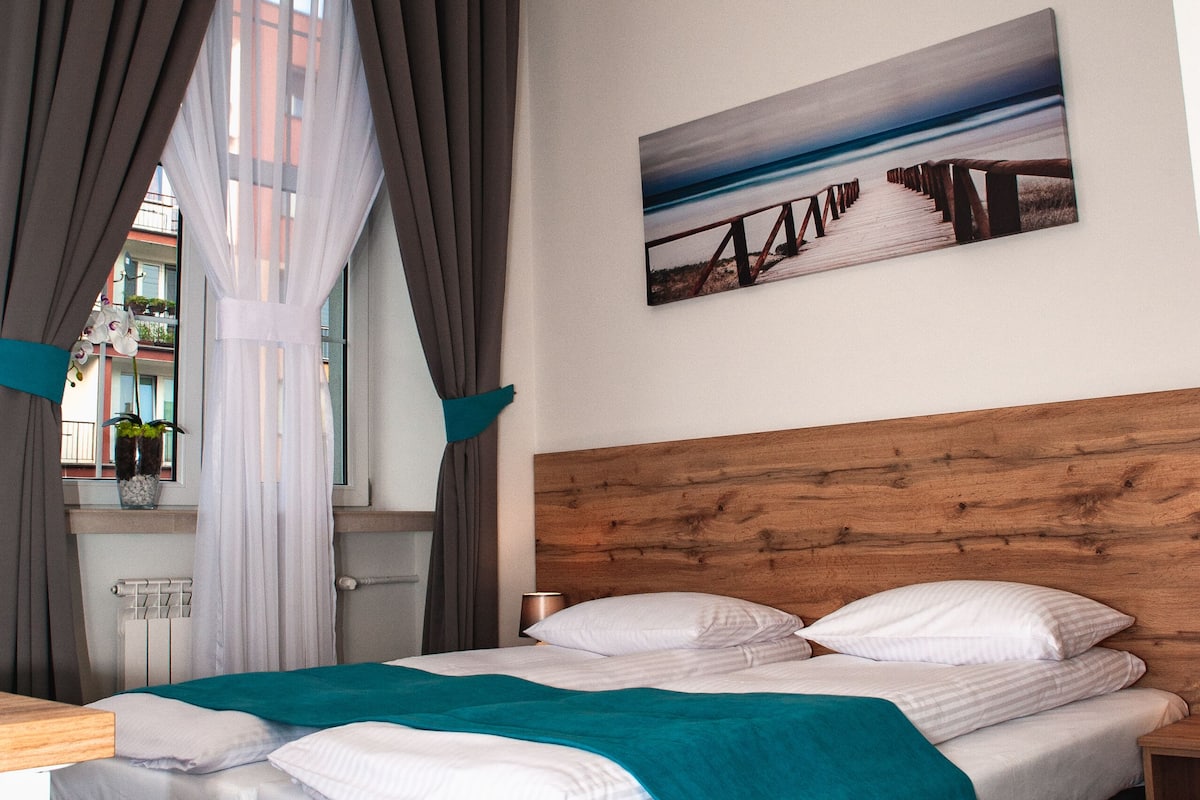 Quarto de hotel com cama, cortinas, um quadro e janela com vista.