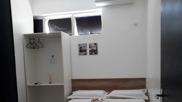 Quarto pequeno e limpo, com uma cama, um guarda-roupa e uma janela.