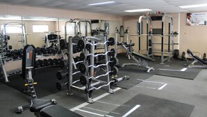 Uma academia com equipamentos de musculação, espelhos e um aviso fixado na parede.