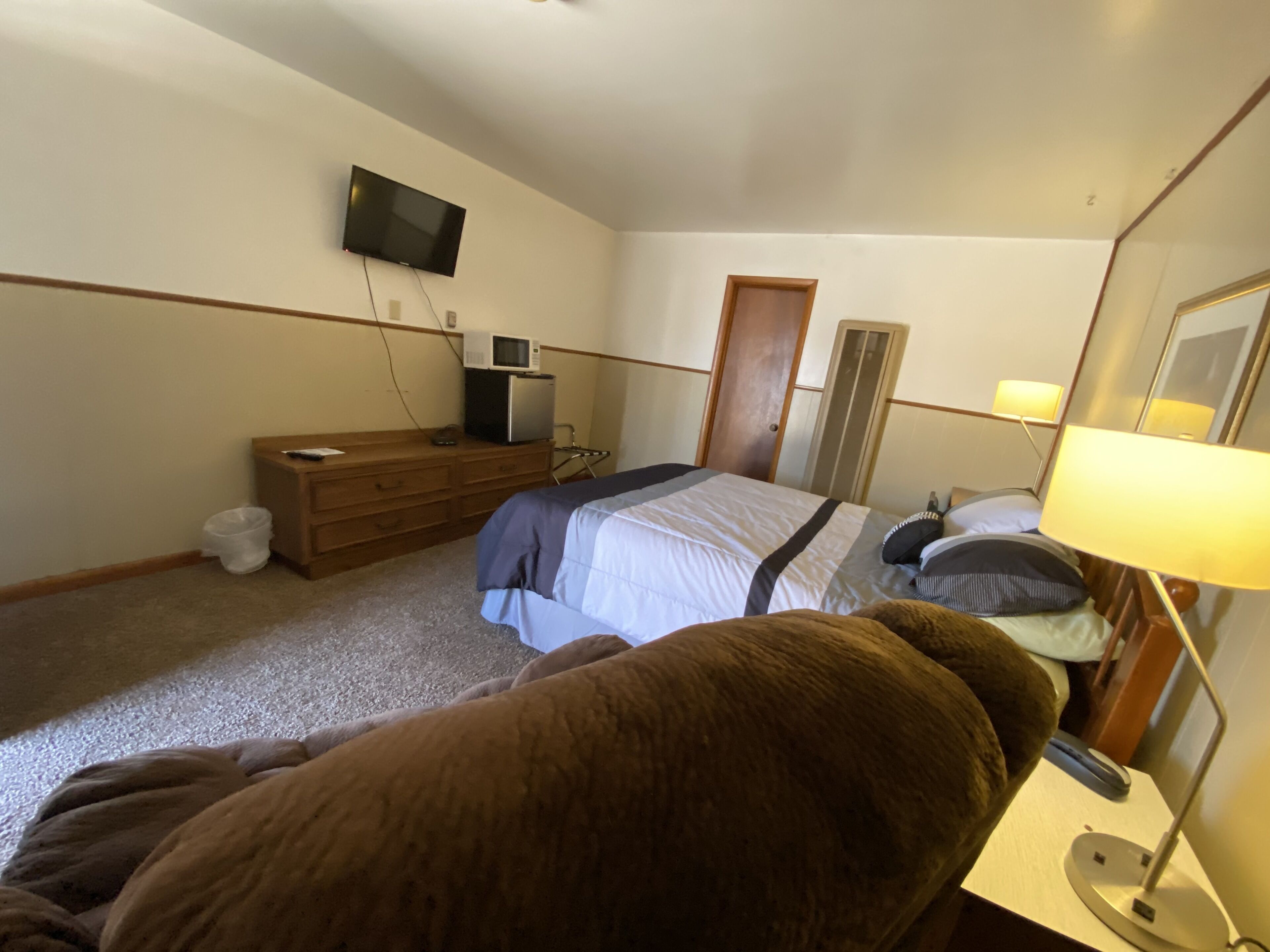Quarto de hotel com cama, penteadeira, televisão na parede, micro-ondas, porta e espelho.