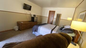 Quarto de hotel com cama, penteadeira, televisão na parede, micro-ondas, porta e espelho.