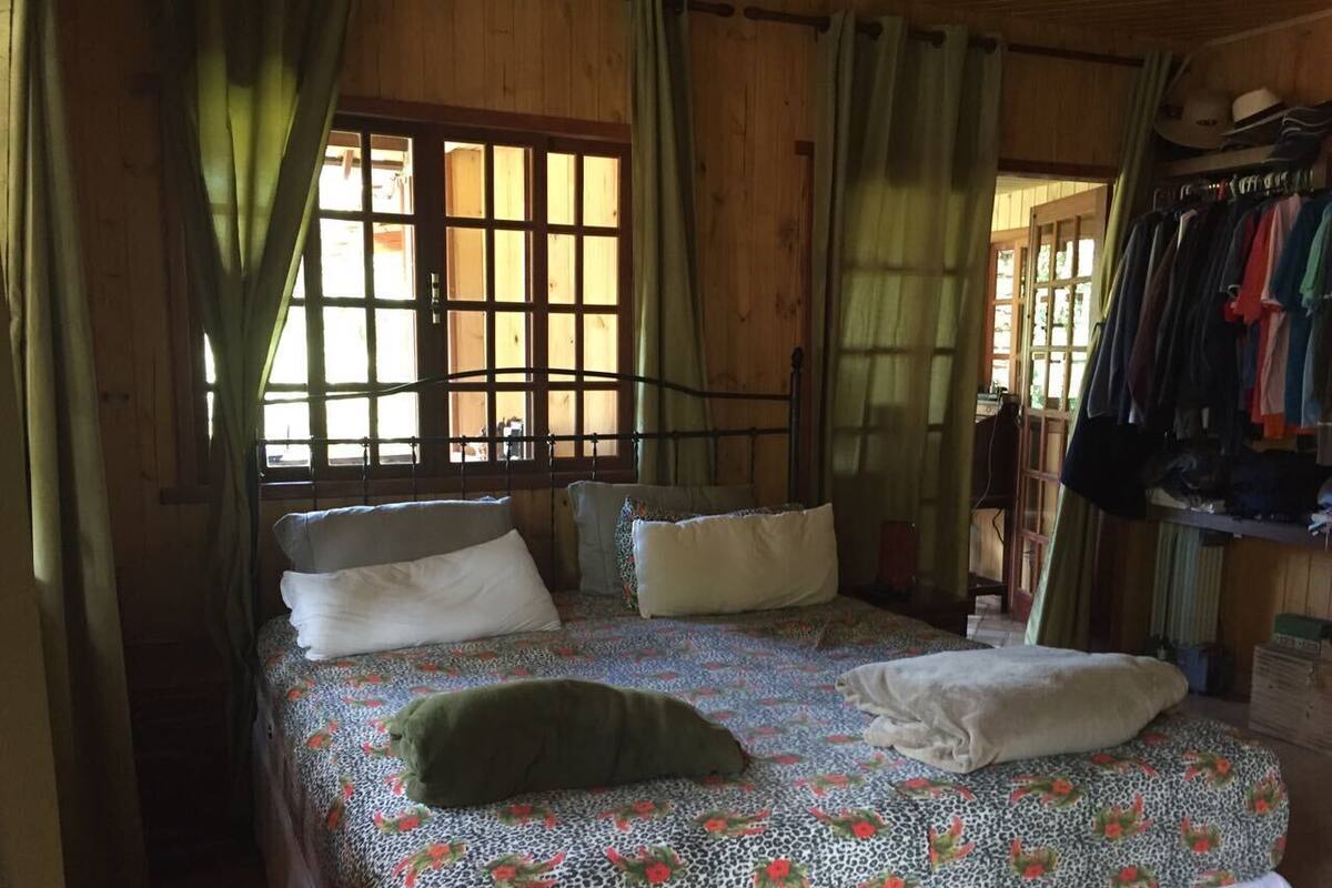 Quarto de madeira com cama, cortinas e um cabideiro.