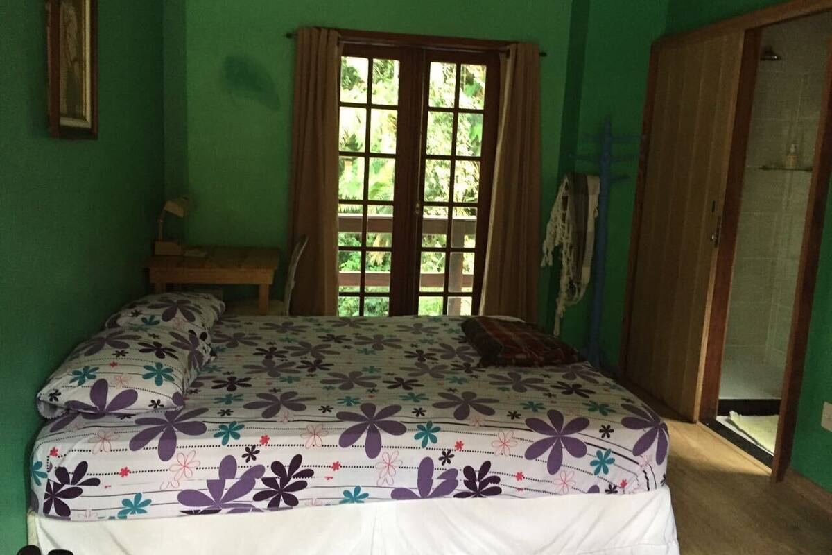 Um quarto com cama, janela com cortinas, porta de madeira e parede verde.