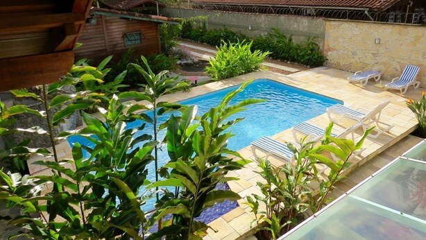 Uma piscina com espreguiçadeiras, cercada por vegetação e um muro de pedra.