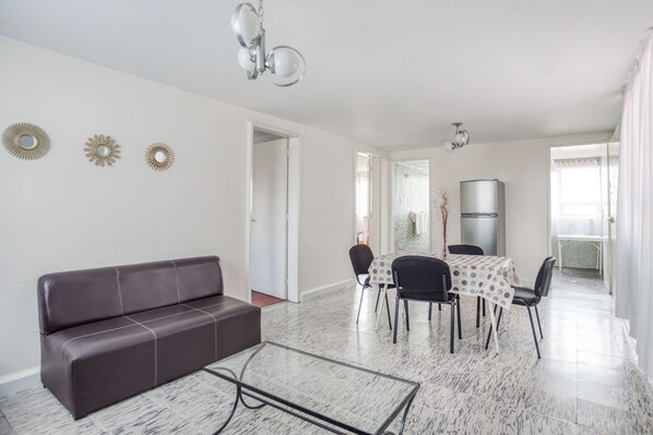 Uma sala de estar moderna com um sofá de couro marrom, uma mesa de centro de vidro e uma área de jantar com toalha de mesa estampada em bolinhas.