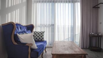 Quarto com sofá azul, mesa de centro de madeira e janela com cortinas leves.
