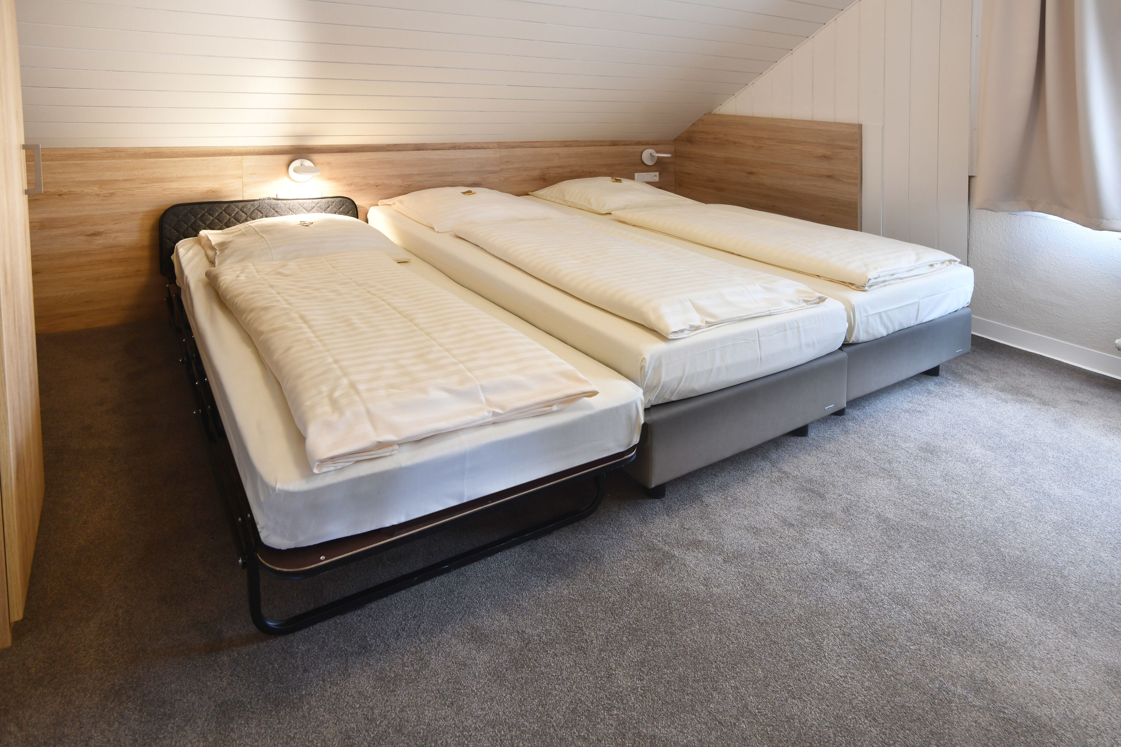 Quarto com duas camas de solteiro, cabeceira de madeira, luminária e janela com cortinas.