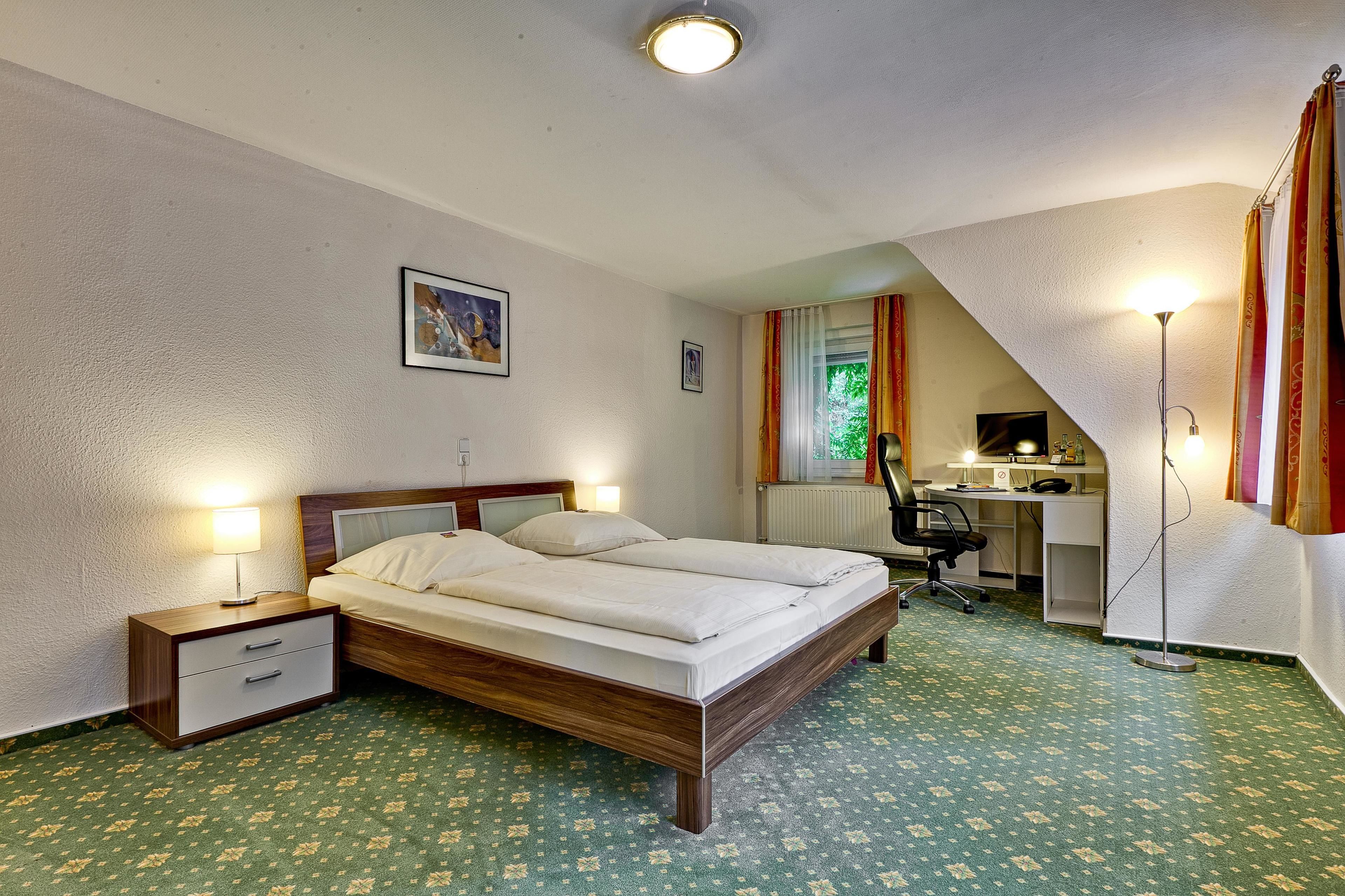 Quarto de hotel com cama, escrivaninha, cadeira e abajur.