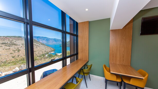 Uma zona de refeições moderna com grandes janelas, uma mesa de madeira e cadeiras amarelas.
