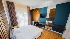 Quarto de hotel moderno com uma cama grande, televisão de tela plana, piso de madeira e um espelho refletindo a decoração do quarto.