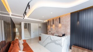 Uma área de recepção moderna com balcão de mármore, teto curvo e escada ao fundo.