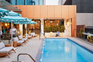 Área de piscina no terraço com espreguiçadeiras, guarda-sóis, bar e vista para a cidade.