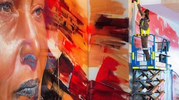 Um mural com arte abstrata e uma pessoa pintando em andaime.
